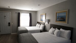 Quarto de hotel com duas camas, uma janela com cortinas, uma porta com uma placa e dois quadros na parede.