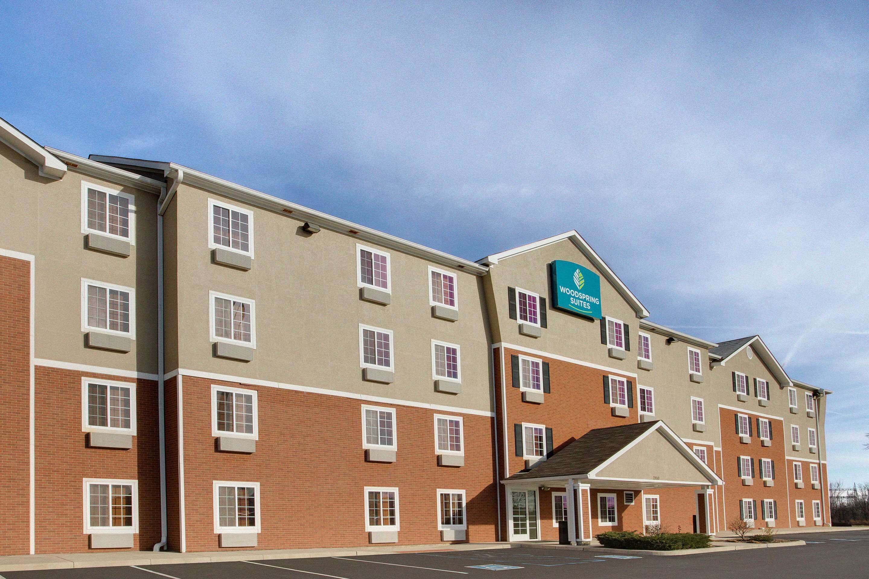 Um hotel de vários andares com fachada de tijolos, diversas janelas e uma placa indicando ser uma unidade Spring Suites.