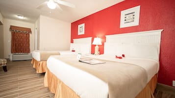 Quarto de hotel com duas camas, um ventilador de teto, parede vermelha e uma janela com cortinas.