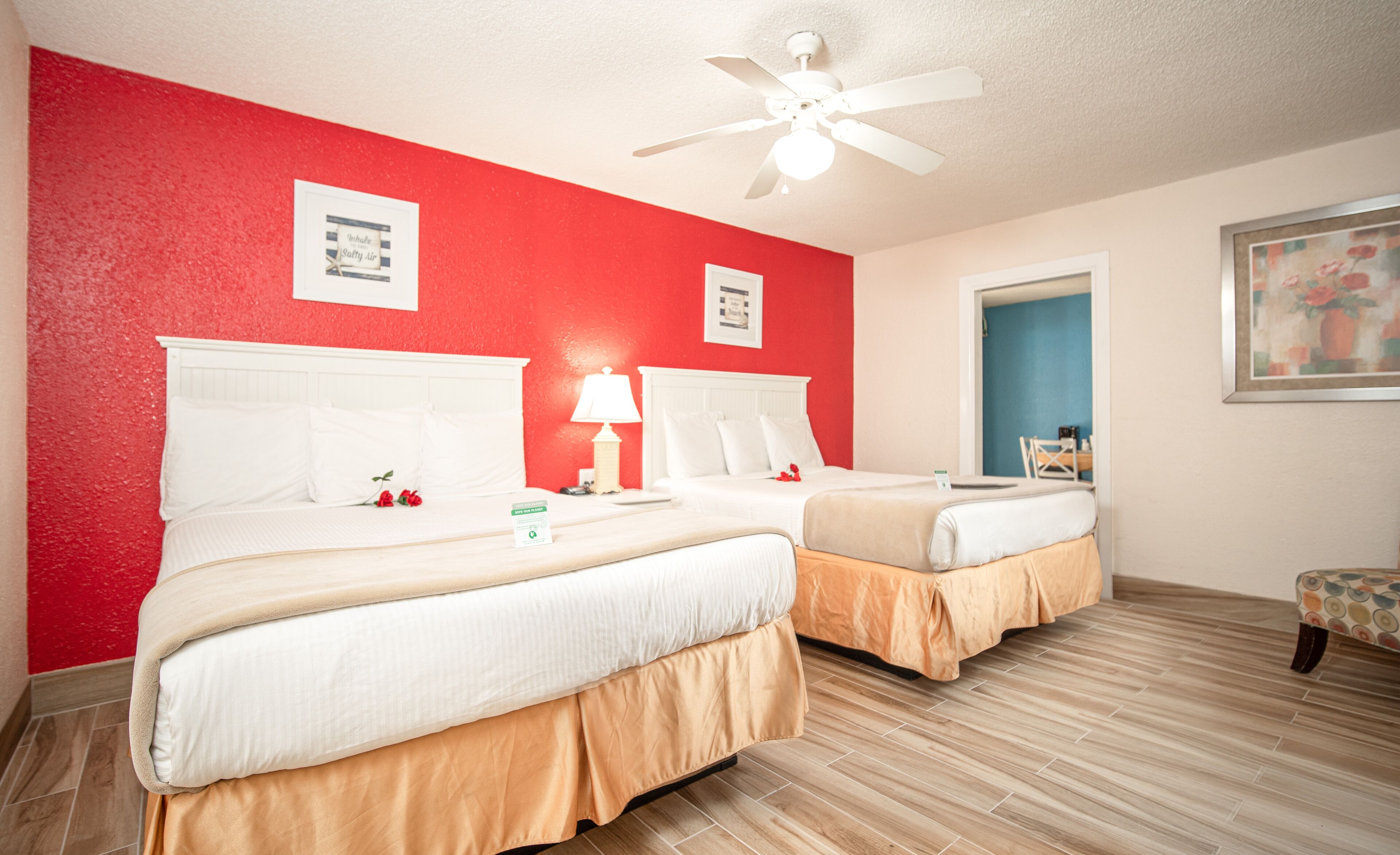 Quarto de hotel com duas camas, ventilador de teto e uma parede em vermelho.