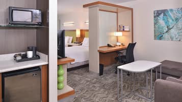 Quarto de hotel com cozinha compacta, cama, escrivaninha, cadeira e mesa pequena.