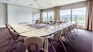 Uma sala de conferências com uma mesa comprida, cadeiras, um projetor e vista para montanhas através de grandes janelas.