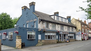 Um pub tradicional chamado 'The Fox Inn', com arquitetura clássica, janelas amplas e porta de madeira.