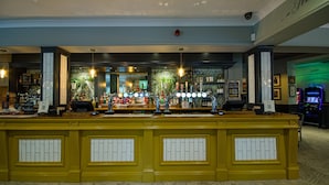 Uma área de bar com balcão, banquetas e diversos tipos de garrafas e copos.