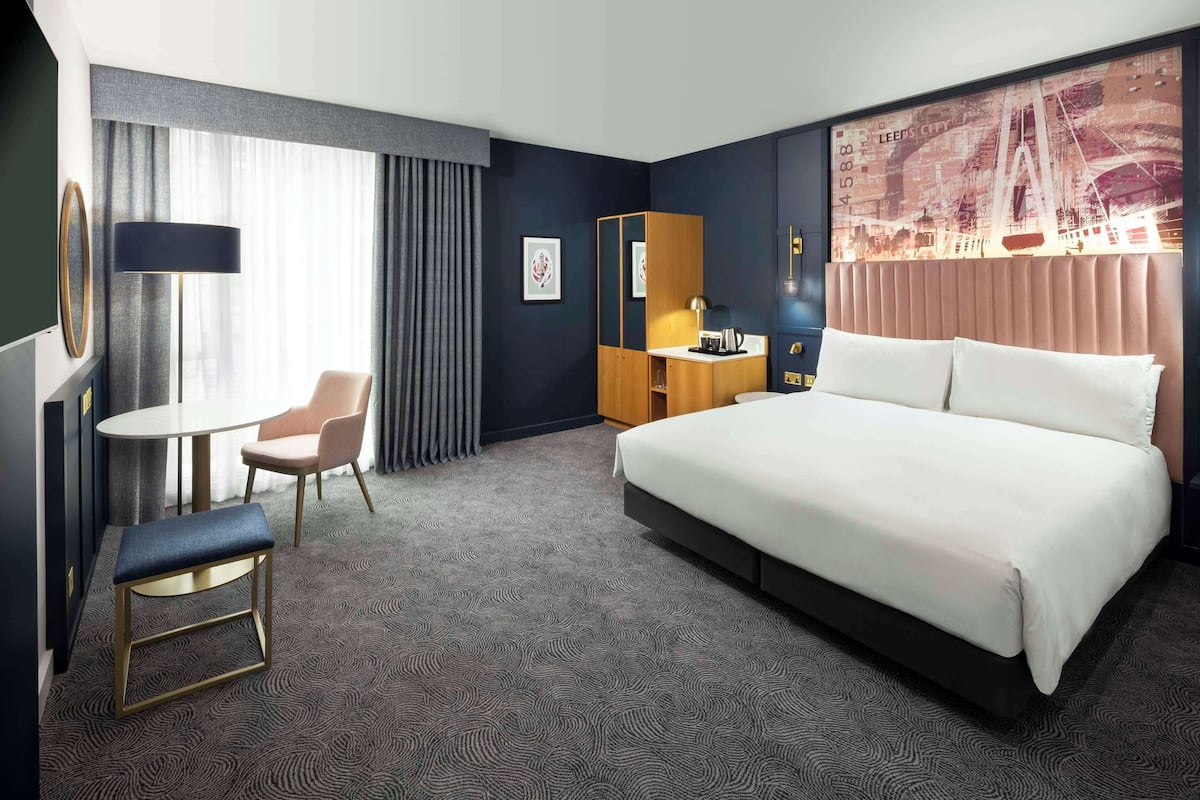 Quarto de hotel com uma cama grande, uma escrivaninha, uma cadeira e uma pequena mesa.