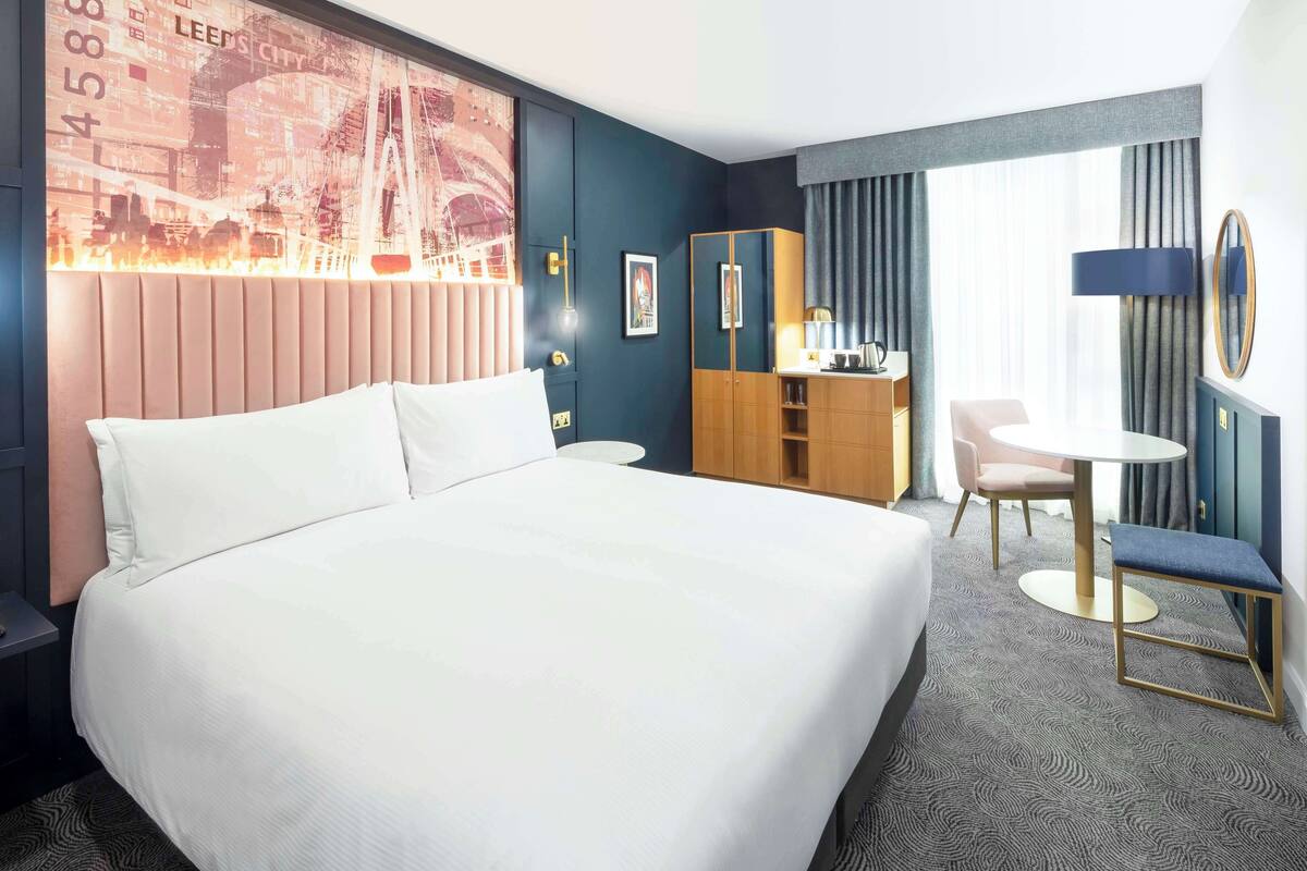 Quarto de hotel com uma cama grande, uma escrivaninha com cadeira, uma mesinha e um guarda-roupa.
