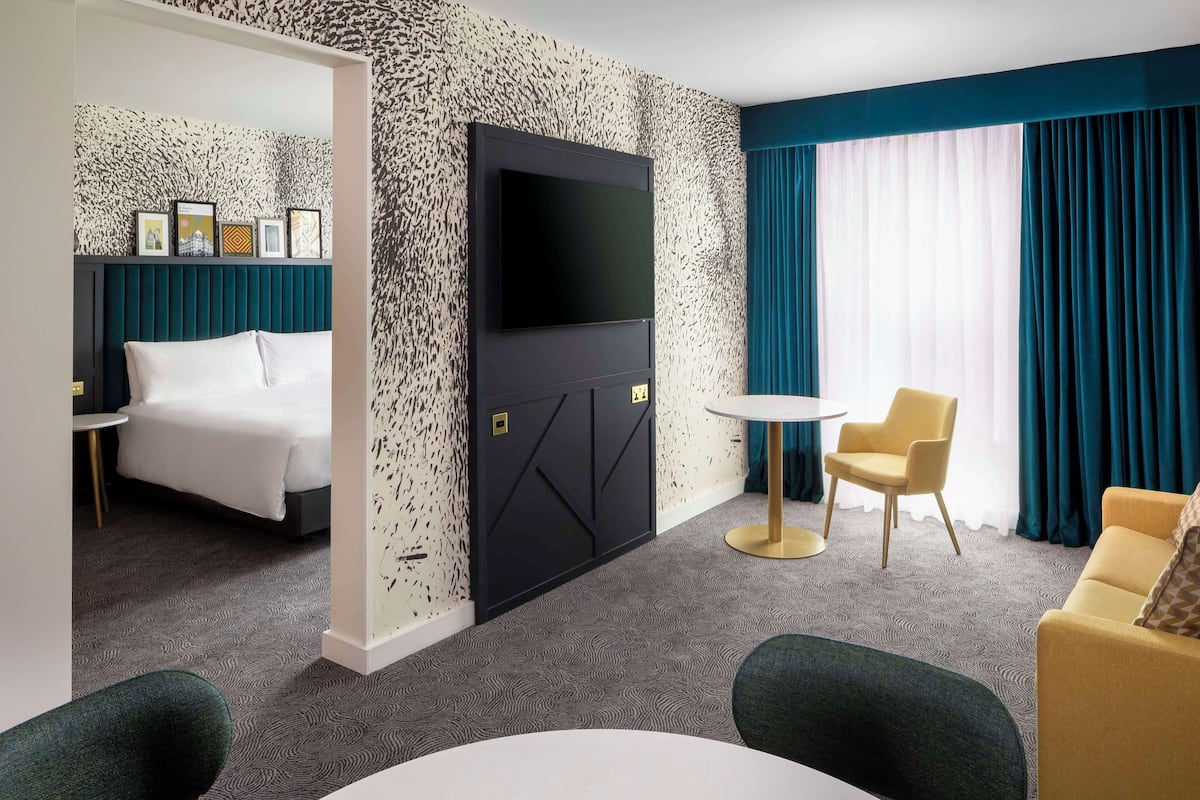 Quarto de hotel com cama, televisão, escrivaninha, cadeira e sofá.