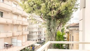 Um edifício residencial com várias andares e varandas, uma grande árvore em primeiro plano, e uma vista ampla da região.
