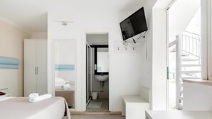 Quarto de hotel moderno com uma cama, uma mesa, uma TV e um banheiro visível por uma porta aberta.