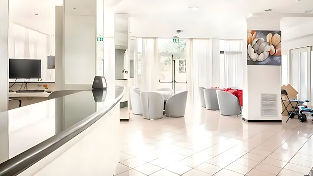 Um lobby moderno de hotel, com balcão de recepção, área de estar e uma grande janela que oferece iluminação natural.