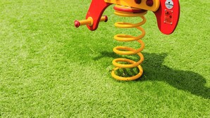 Um parquinho com um balanço vermelho e amarelo e uma estrutura de escalada verde.