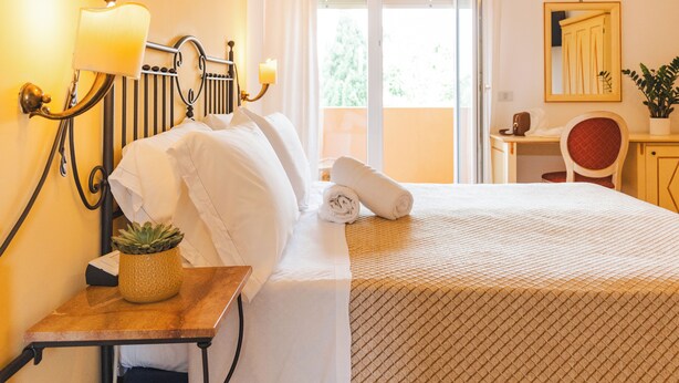Quarto de hotel com cama, mesa de cabeceira, luminária e vista para o exterior.