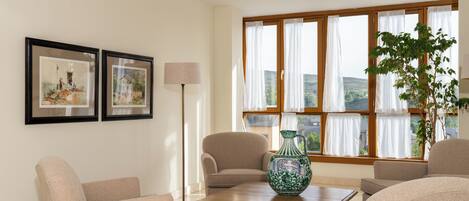 Sala de estar com sofá, mesa de centro, abajur e uma grande janela com cortinas.