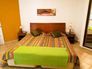 Uma cama com colcha estampada e duas almofadas, cabeceira de madeira e um quadro na parede.