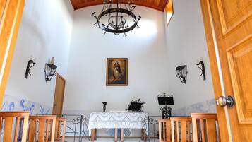 Interior de capela com altar de madeira, bancos, lustre e pintura na parede.
