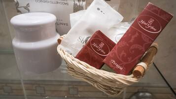 Cesto com itens da marca Hotel Grifone, um recipiente cerâmico branco e um saco plástico branco.