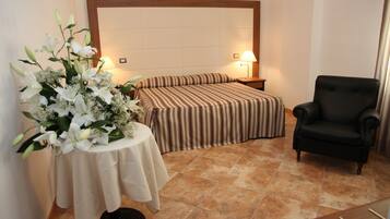 Quarto de hotel com cama, uma cadeira, mesa com flores e duas luminárias de cabeceira.