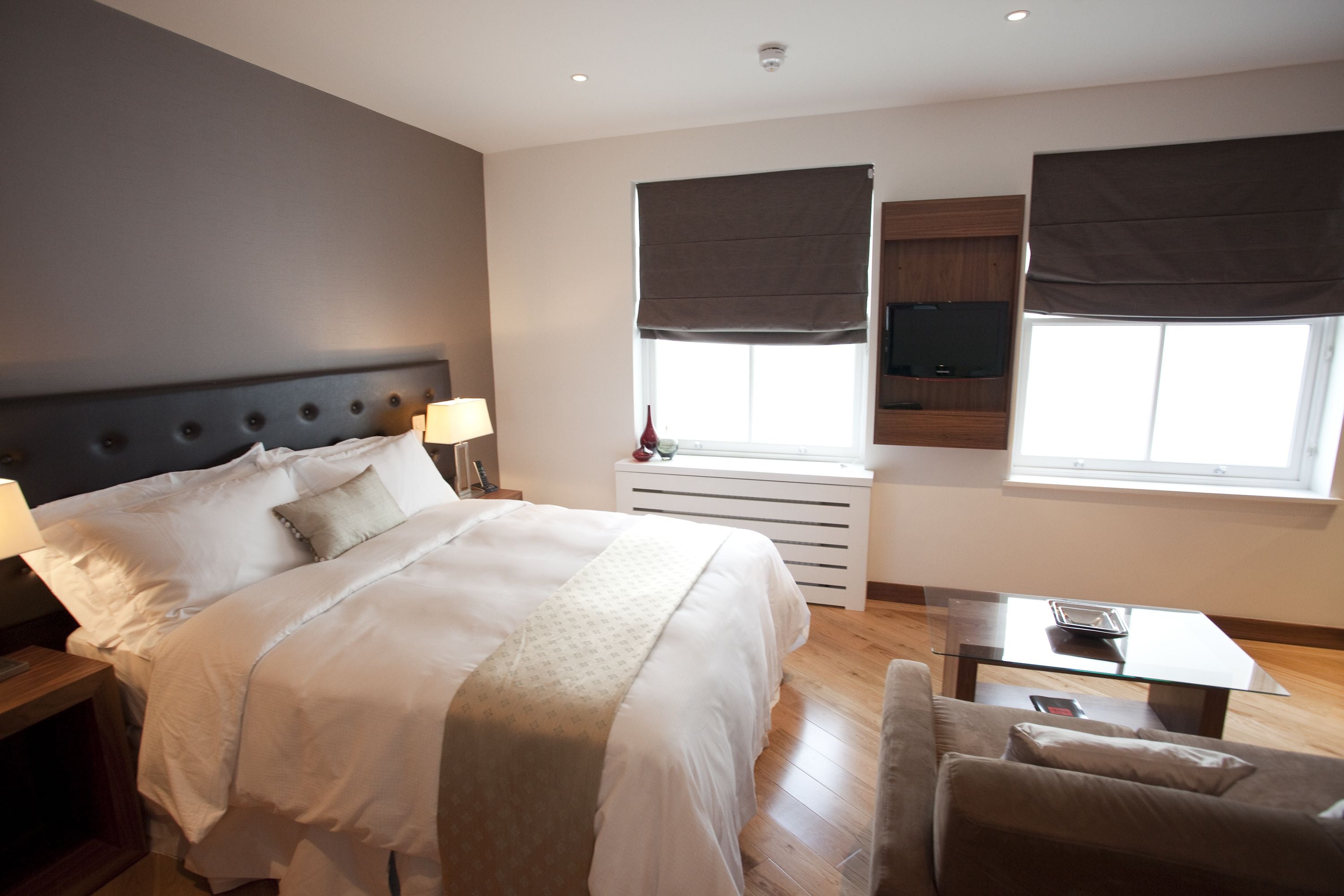 Quarto moderno com cama grande, mesas de cabeceira, televisão e uma mesinha.