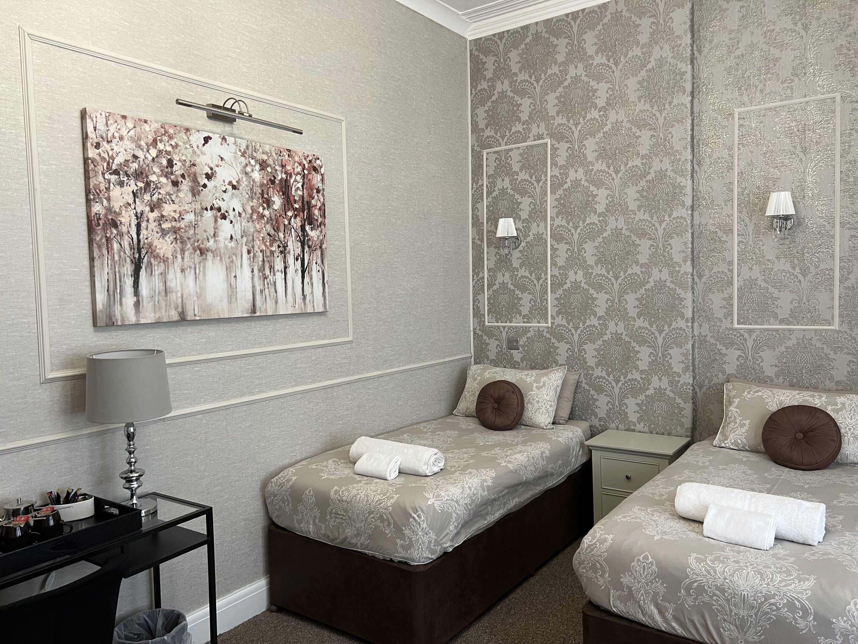 Quarto de hotel com duas camas, uma escrivaninha e um quadro grande na parede.