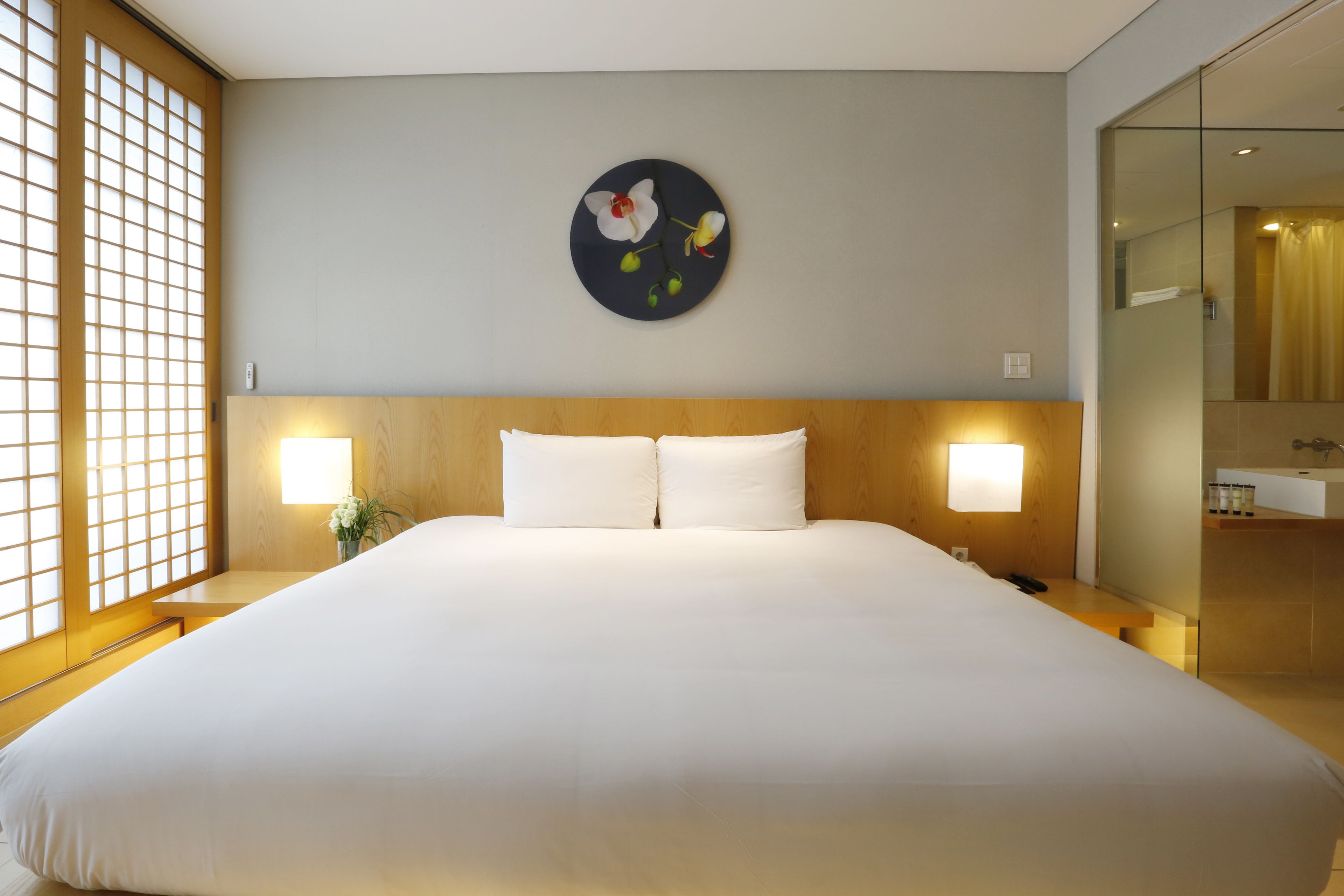 Quarto de hotel com uma cama grande, duas luminárias de cabeceira, um relógio de parede e uma janela com vista para o exterior.