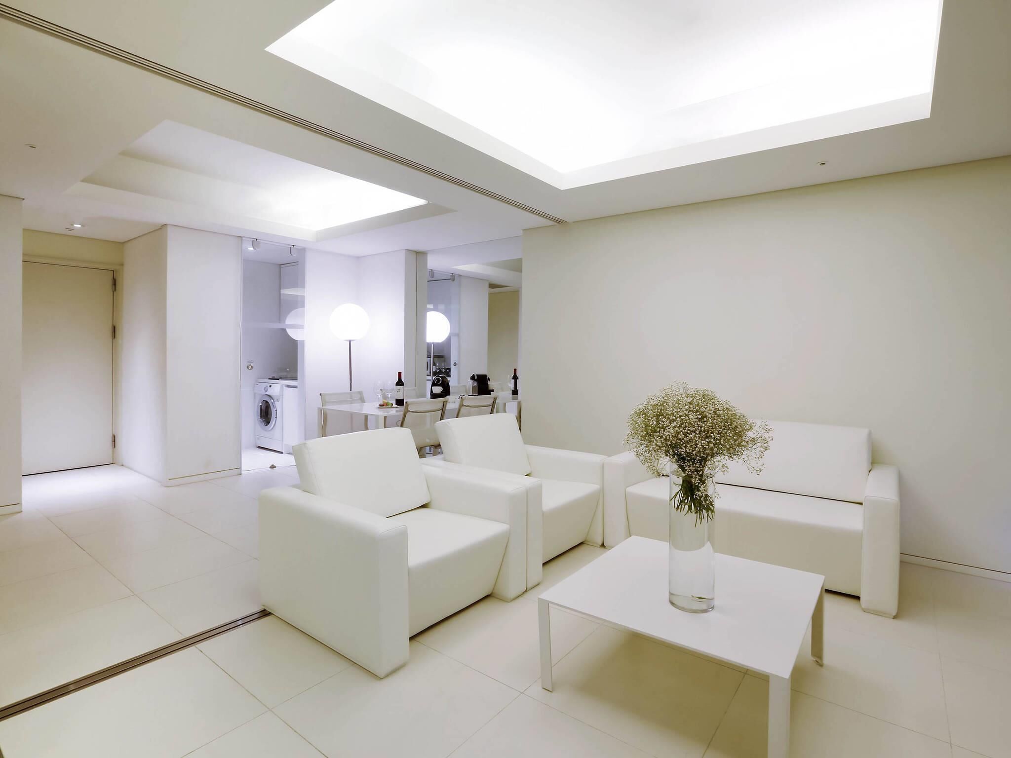 Uma sala de estar moderna com decoração em branco, um sofá, uma mesa de centro e um vaso com flores.