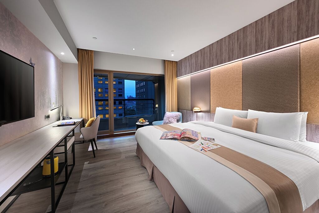 Quarto de hotel moderno com uma cama grande, uma escrivaninha e uma televisão.