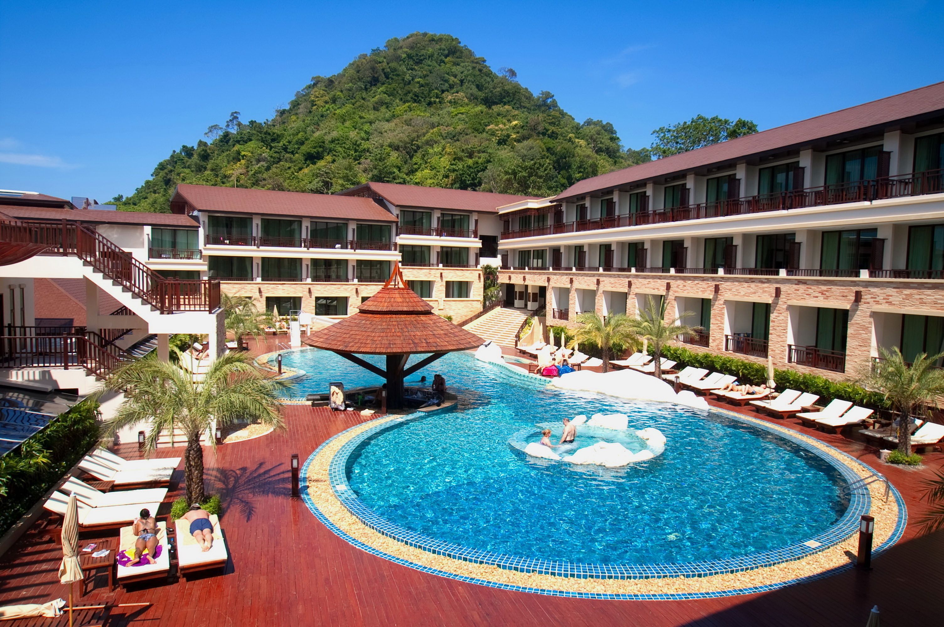 Hotel com uma piscina grande, várias varandas e um cenário montanhoso.