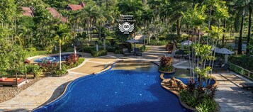 Área de piscina de resort com hidromassagem, espreguiçadeiras e paisagismo tropical.