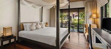 Uma cama com dossel e roupa de cama branca, uma televisão sobre um armário de madeira, e uma varanda com mobiliário exterior.