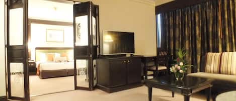 Quarto de hotel com cama, televisão, sofá e mesa de centro.