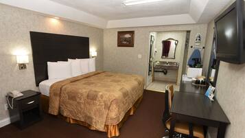 Quarto de hotel com uma cama grande, uma mesa, uma cadeira, telefone, espelho e televisão.
