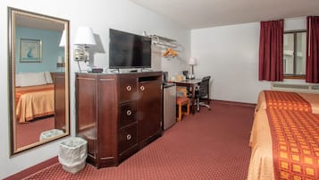 Quarto de hotel com uma cama grande, cômoda, escrivaninha com cadeira, televisão e espelho.