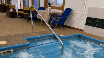Uma piscina termal com escada de metal, cadeiras azuis e aviso proibindo animais de estimação na área da piscina.