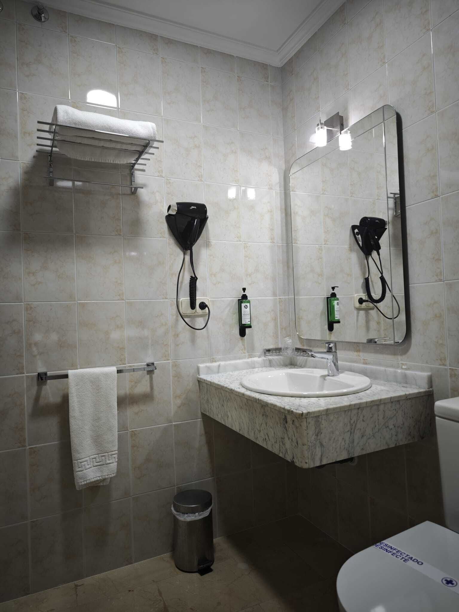 Casa de banho com lavatório, espelho, porta-toalhas e secador de cabelo.