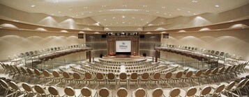Sala de conferências com palco, assentos dispostos em semicírculo e uma grande tela exibindo o logotipo da Hilton.