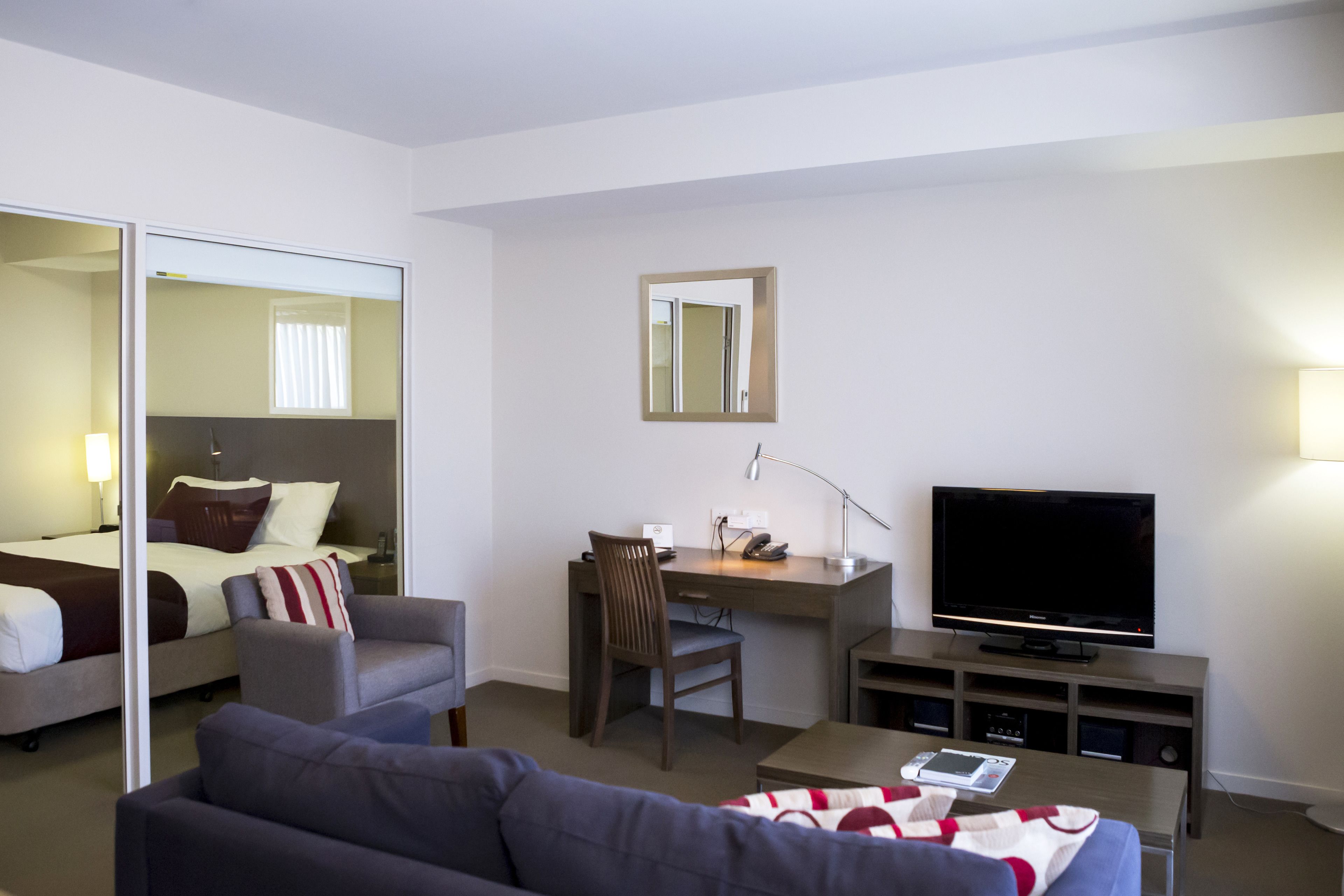 Quarto de hotel com cama, escrivaninha, televisão, sofá e espelho.