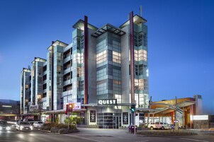 Um hotel moderno com uma fachada de vidro e um letreiro chamativo com a palavra 'QUEST', além de vários andares.
