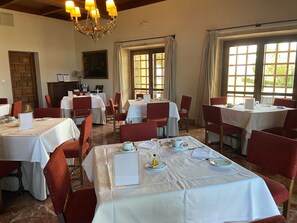 Uma sala de jantar com mesas preparadas para o serviço, cadeiras vermelhas e um lustre.