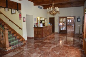 Um hall amplo com piso de mármore, escada de madeira e balcão de recepção.