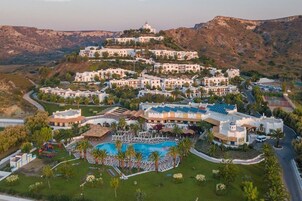 Um resort com vários edifícios, piscina e montanhas ao fundo.