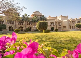 Um hotel com fachada simétrica, várias varandas e um jardim bem cuidado com plantas floridas.