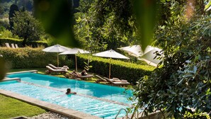 Piscina com espreguiçadeiras e guarda-sóis, rodeada por vegetação.