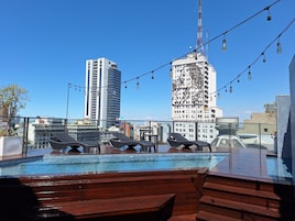 Piscina no terraço com espreguiçadeiras e vista para edifícios da cidade.