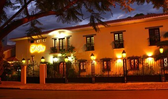 Um hotel com fachada acolhedora, um letreiro iluminado em destaque e entrada com portão.