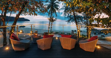 Uma área de estar tranquila ao ar livre, com móveis de vime e vista para o oceano ao entardecer.