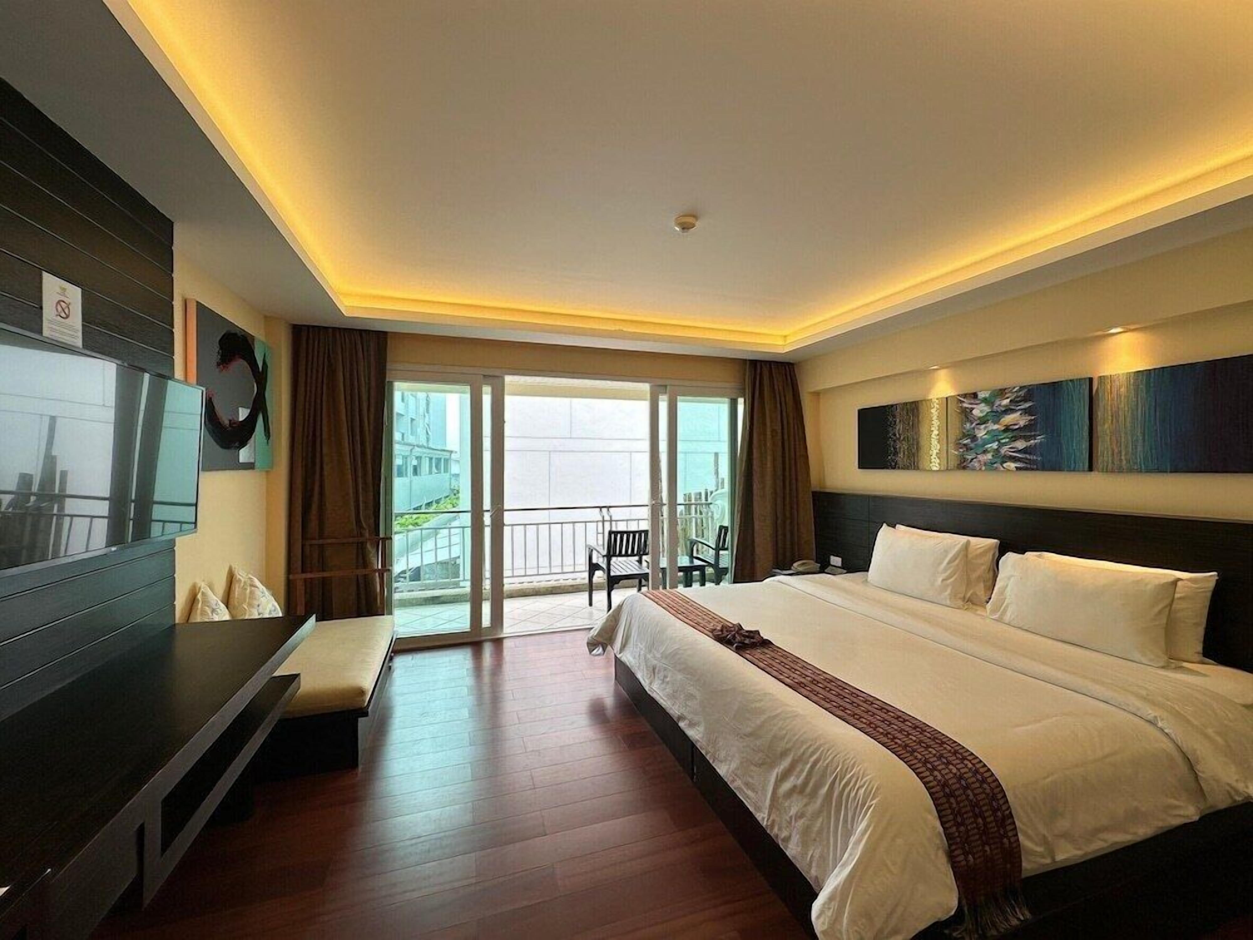 Quarto de hotel com uma cama grande, televisão, varanda com cadeira e um quadro na parede.