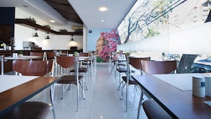 Interior de restaurante moderno com mesas e cadeiras altas, uma grande janela com vista para a cidade e um mural de uma cerejeira rosa.