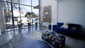 Um lobby moderno com parede de vidro, sofá azul, mesa de vidro e um banquinho estampado.