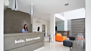 Uma área de recepção moderna com um balcão cinzento identificado com a inscrição “hola. bienvenido”.