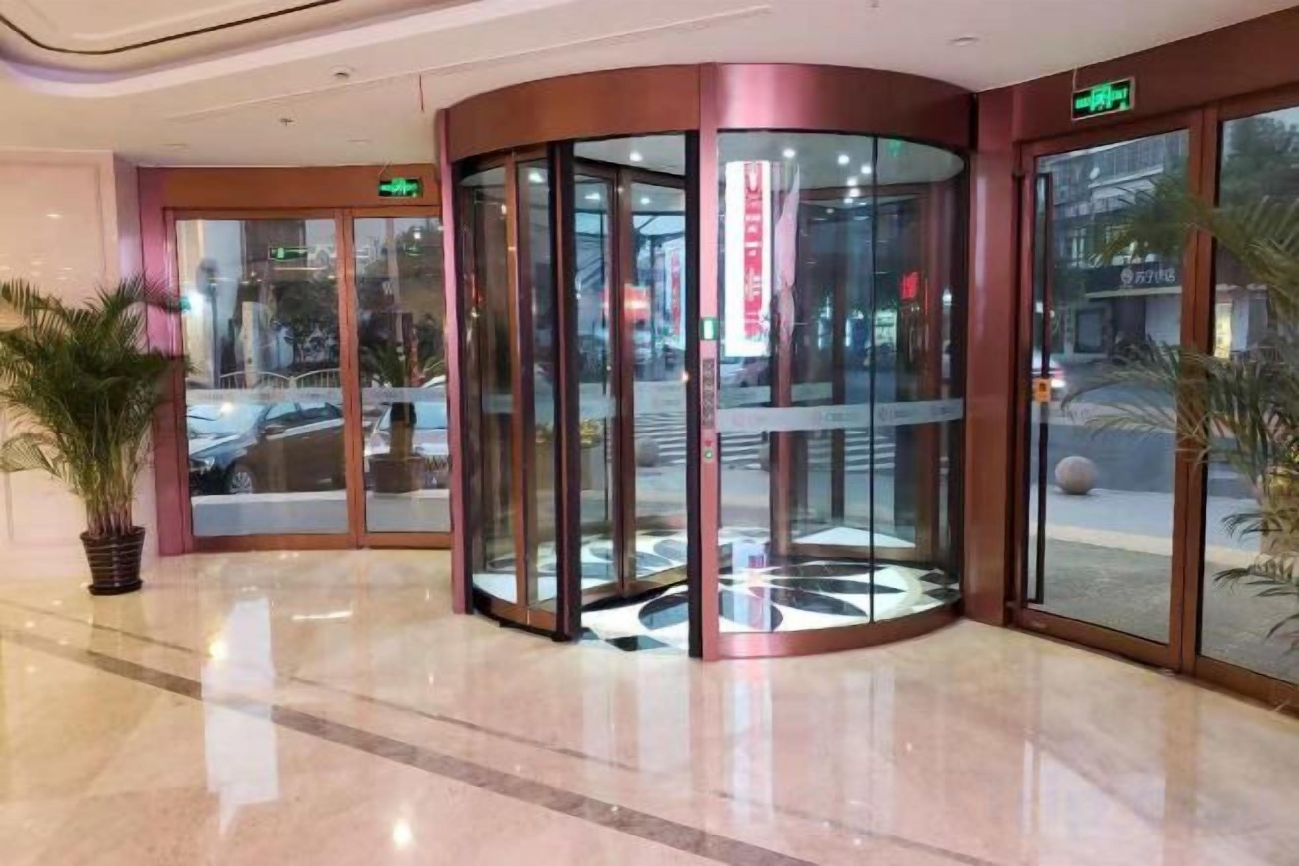 Entrada com portas giratórias de vidro, um vaso de planta e piso limpo e brilhante.